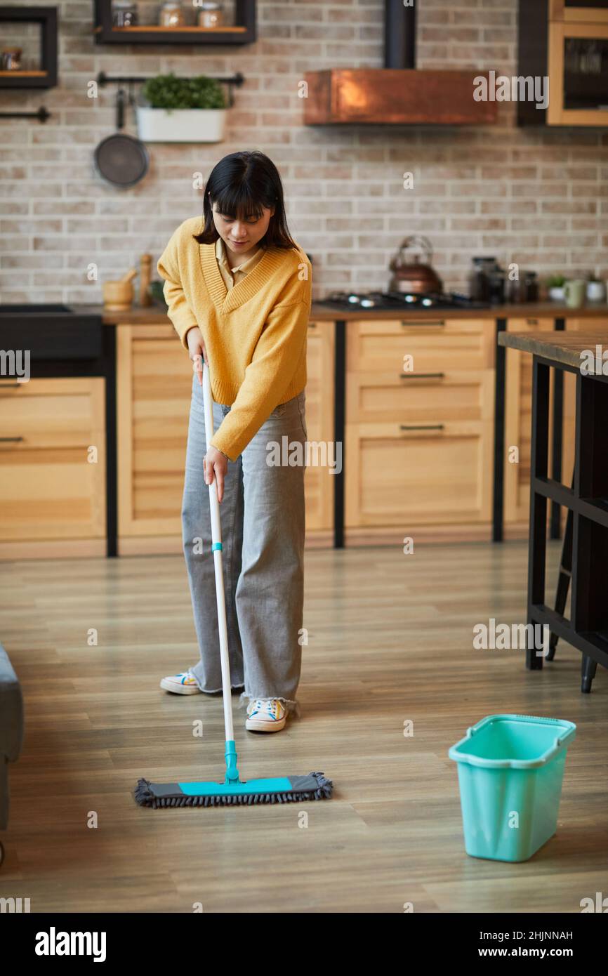 Vertical full length portrait of young Asian woman mopping floors while ...