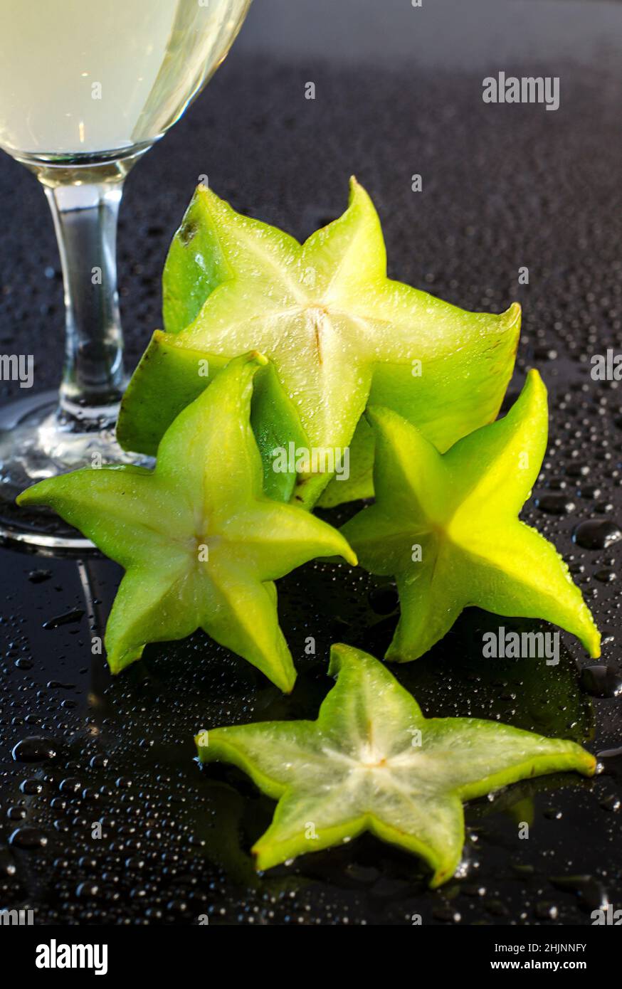 fresh starfruit and a drink in a glass on a black background with water ...