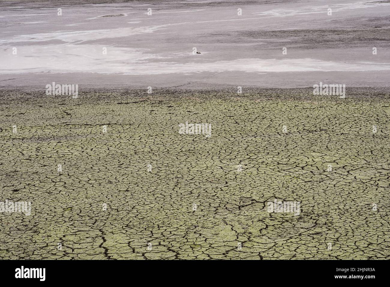 Cracked earth with remnants of silt and frozen water in the background ...