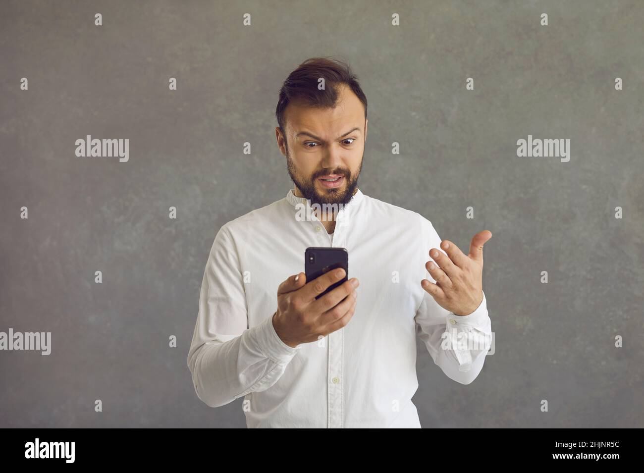 Confused angry annoyed man using smartphone standing over grey ...