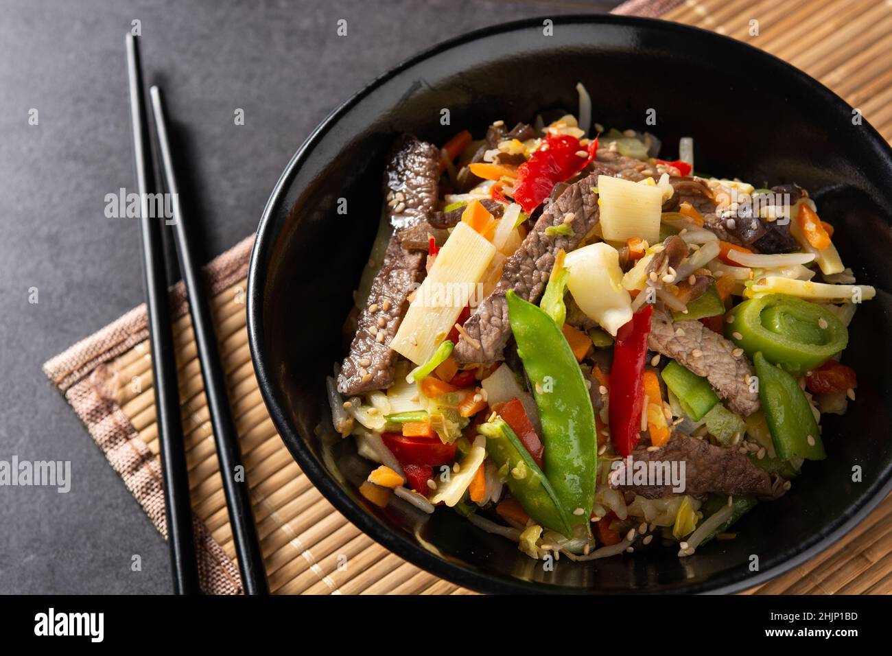 Beef, vegetables and sesame seeds in black bowl on black slate ...