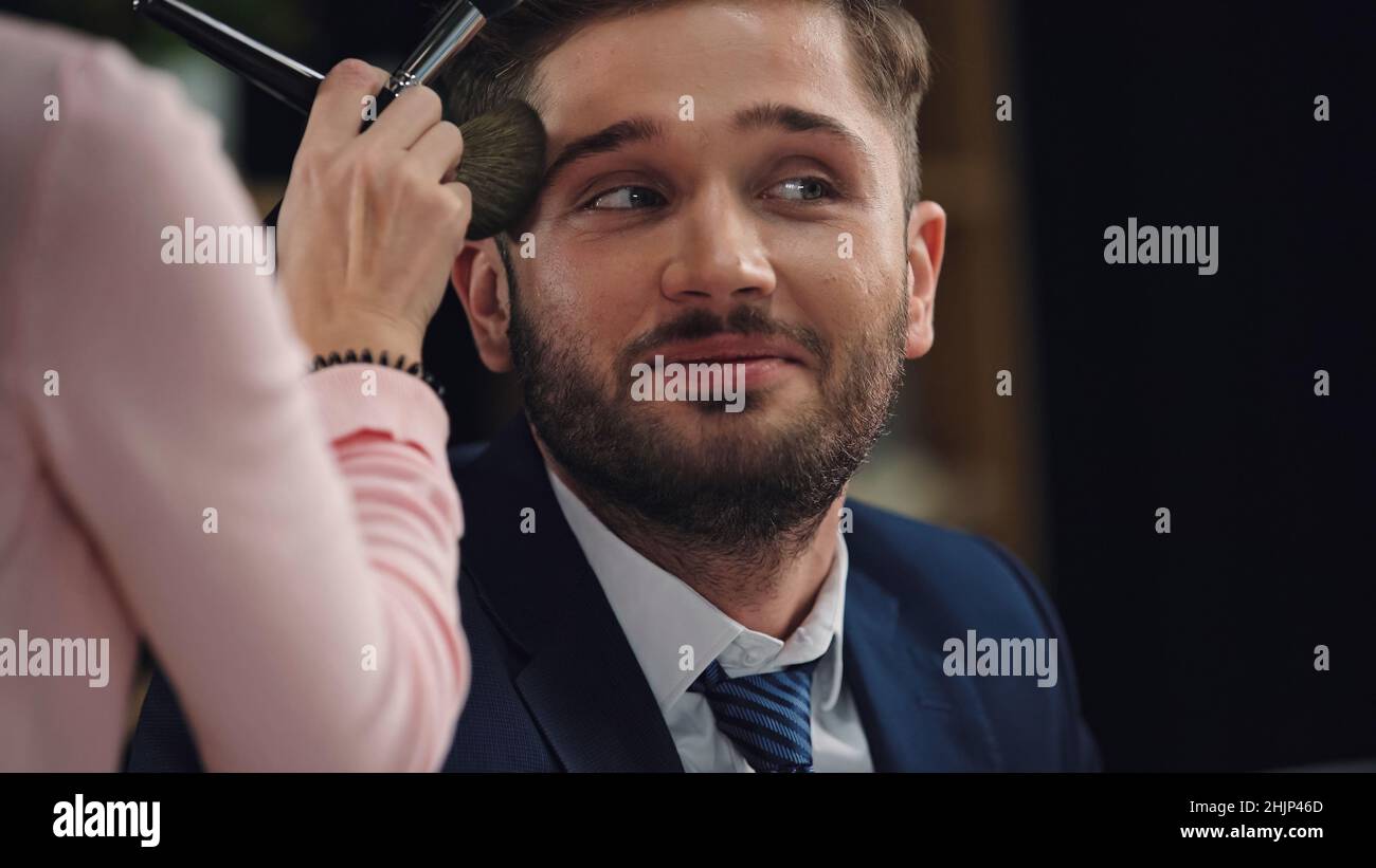 blurred makeup artist applying face powder on smiling man in formal ...