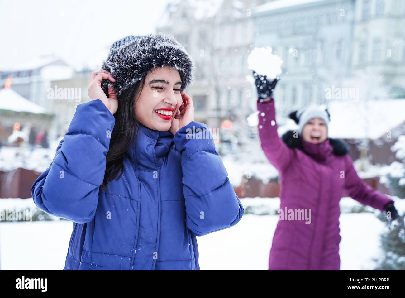 Happy friends play snowballs in winter. Two cheerful women are having ...