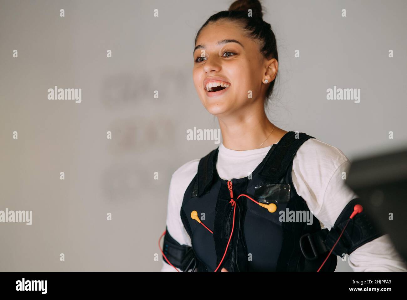 EMS training. Ecstatic girl performs exercises in a suit with cables ...