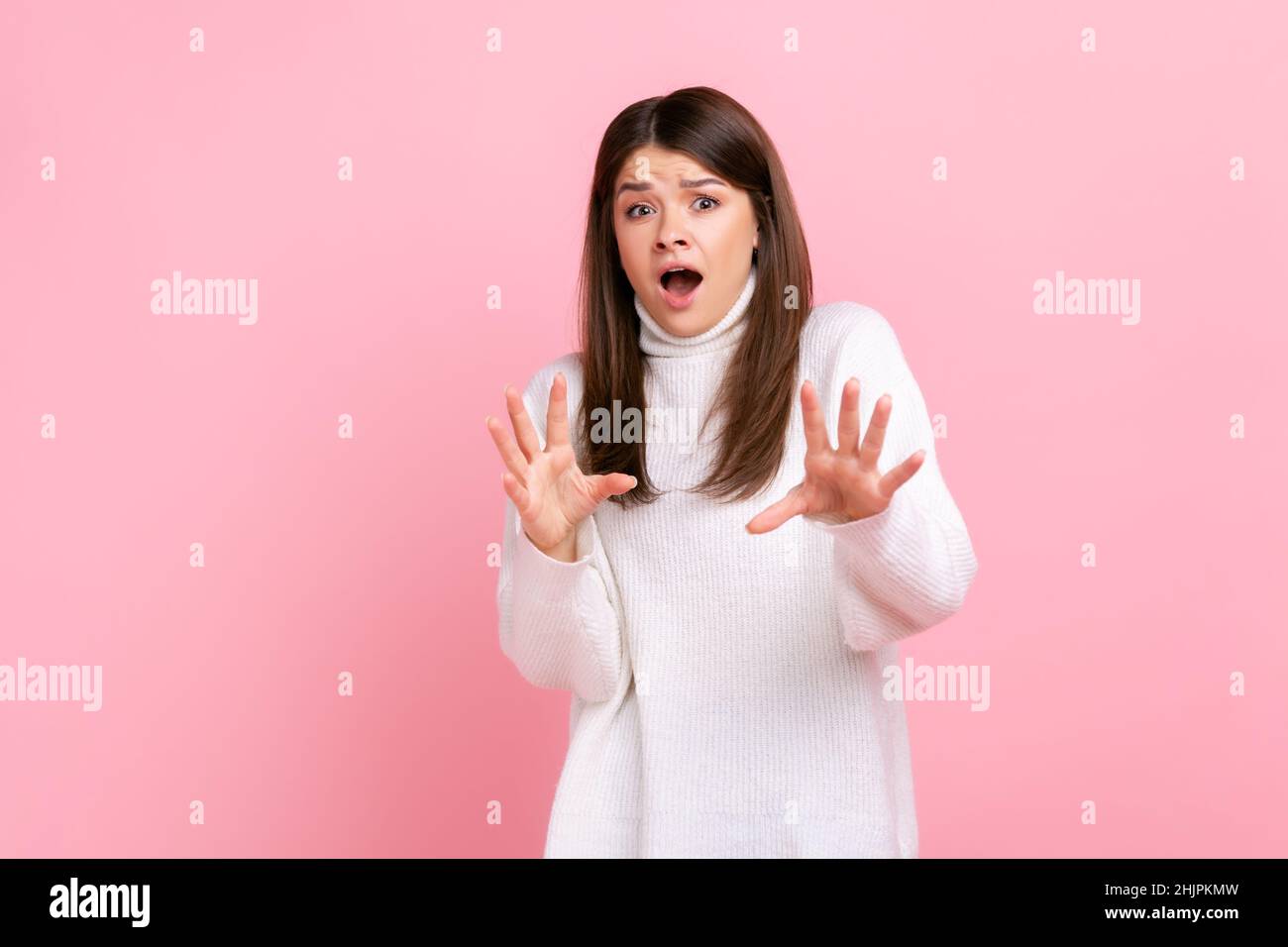 Portrait of scared brunette female stands with raised arms and eyes ...