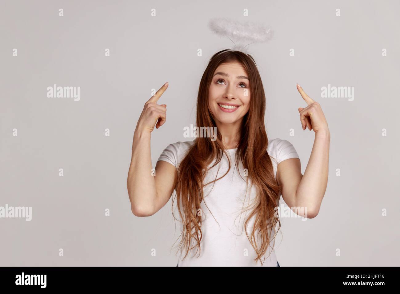 Portrait of positive joyful woman pointing at holy nimbus over head ...