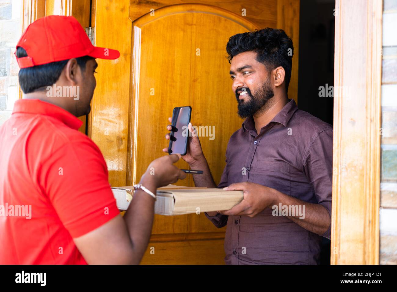 young indian customer showing mobile after paying to delivery boy by ...