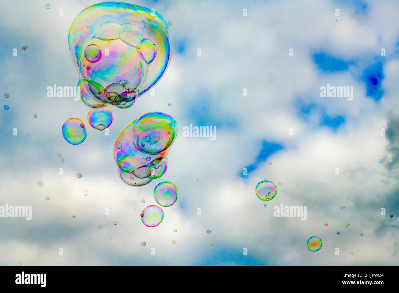 Large colourful soap bubbles blown into a blue sky with white fluffy ...