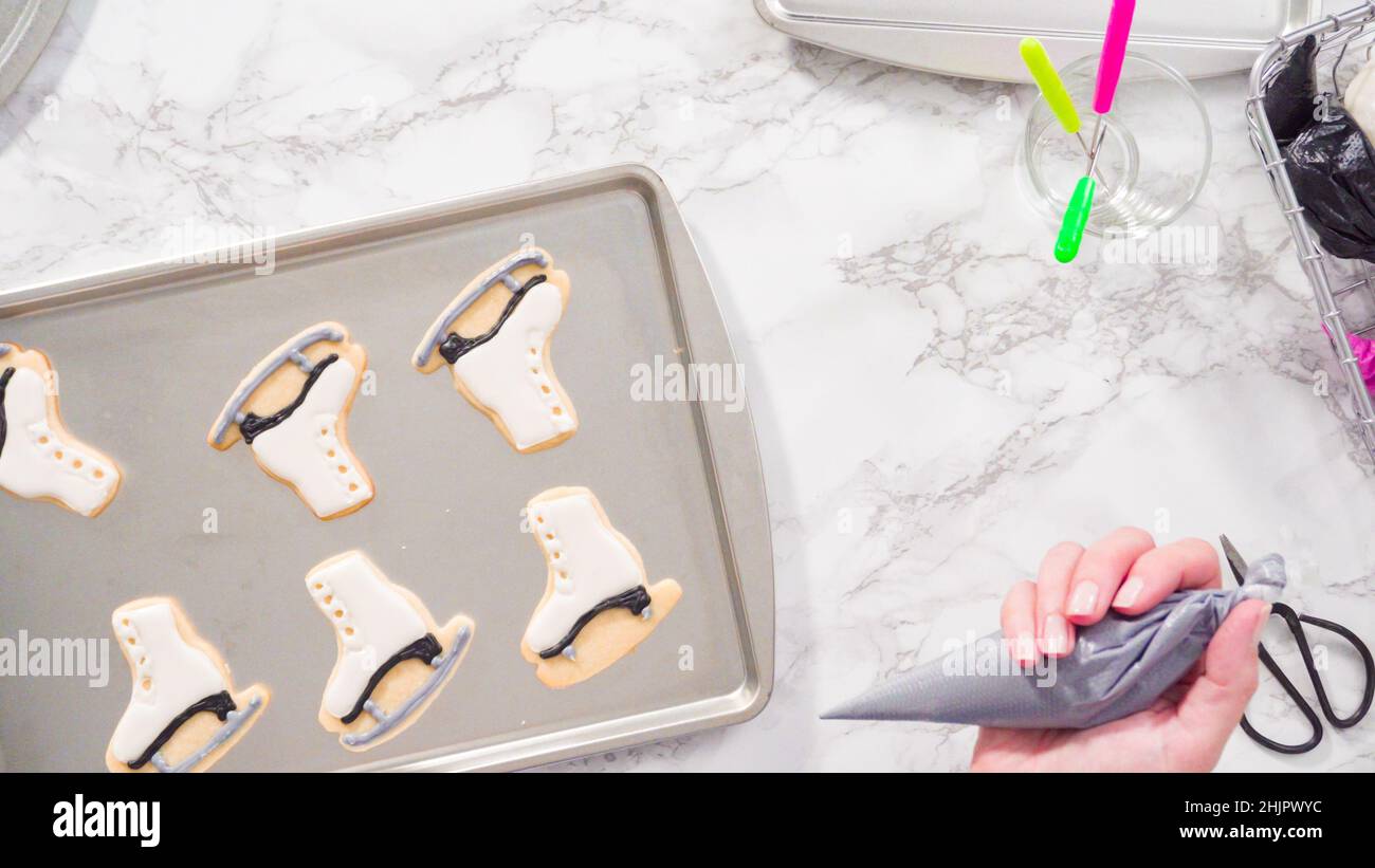 Flat lay. Decorating ice skate shaped sugar cookies with black color ...