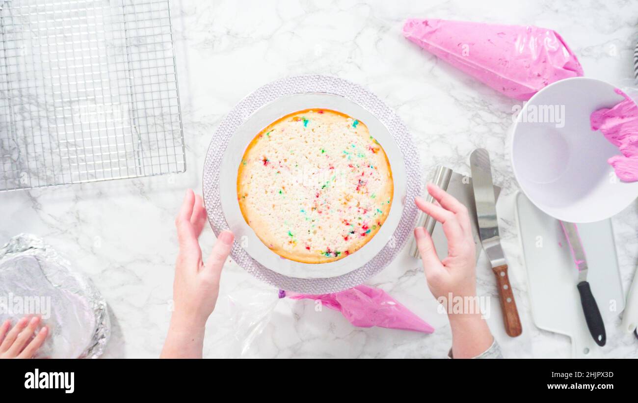 Flat lay. Step by step. Frosting round funfetti cake layers with pink ...