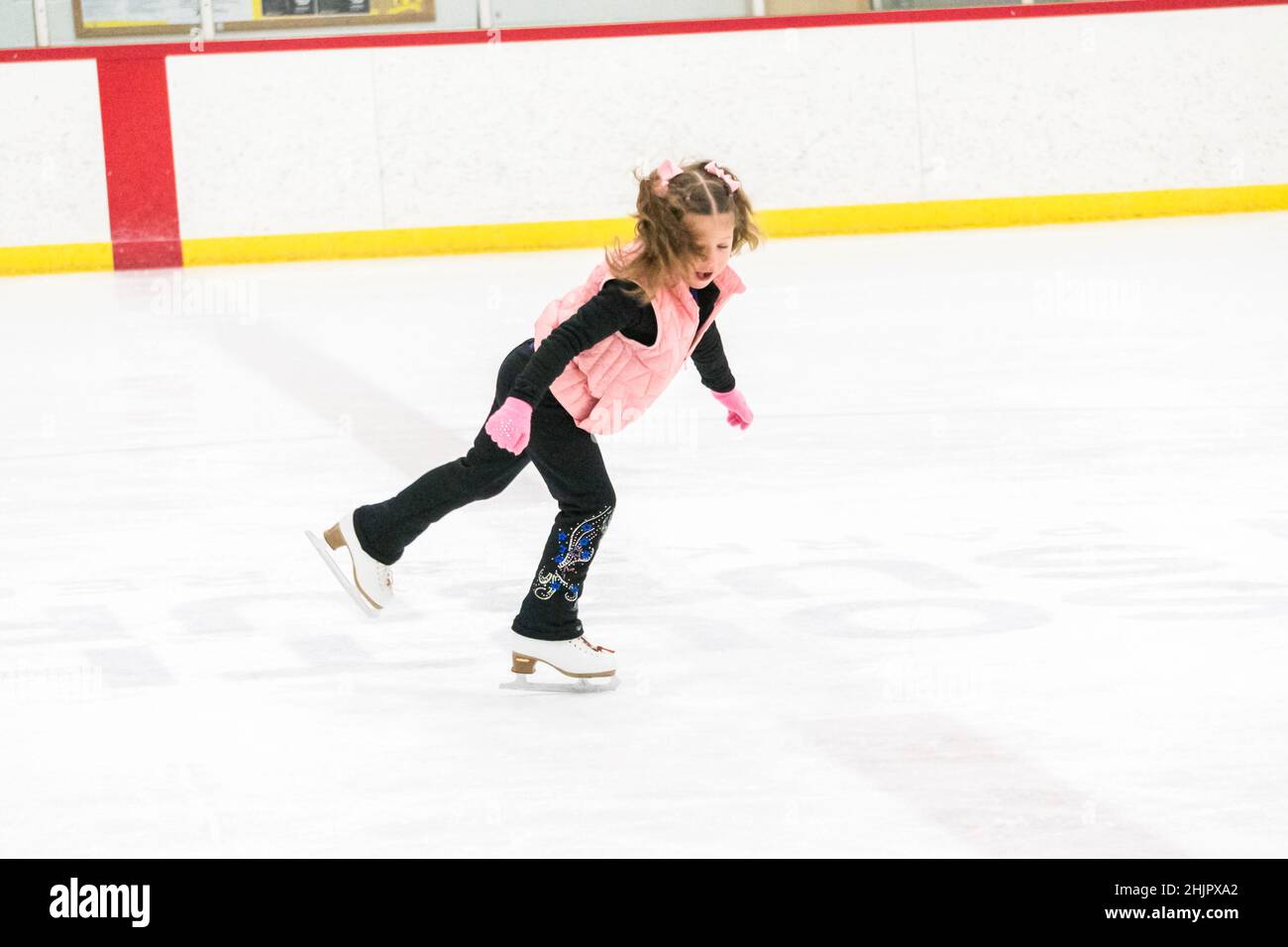 Little girl practicing figure skating moves on the indoor ice rink ...