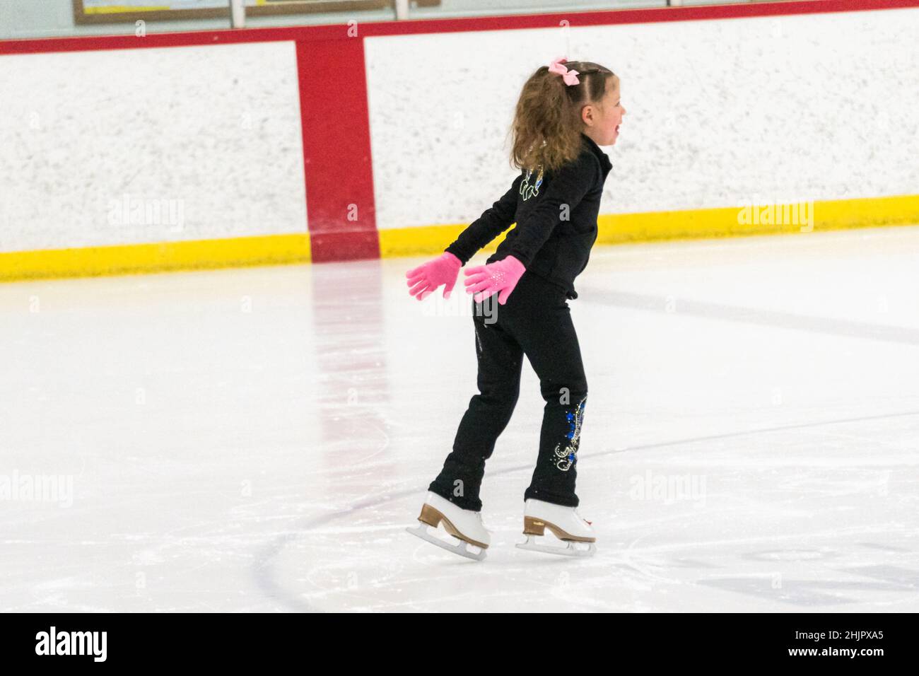 Little girl practicing figure skating moves on the indoor ice rink ...