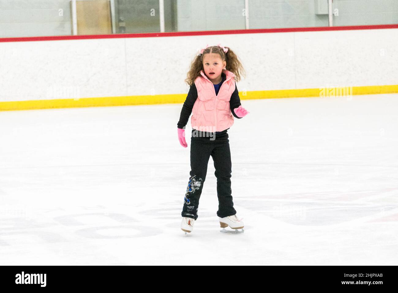 Little girl practicing figure skating moves on the indoor ice rink ...