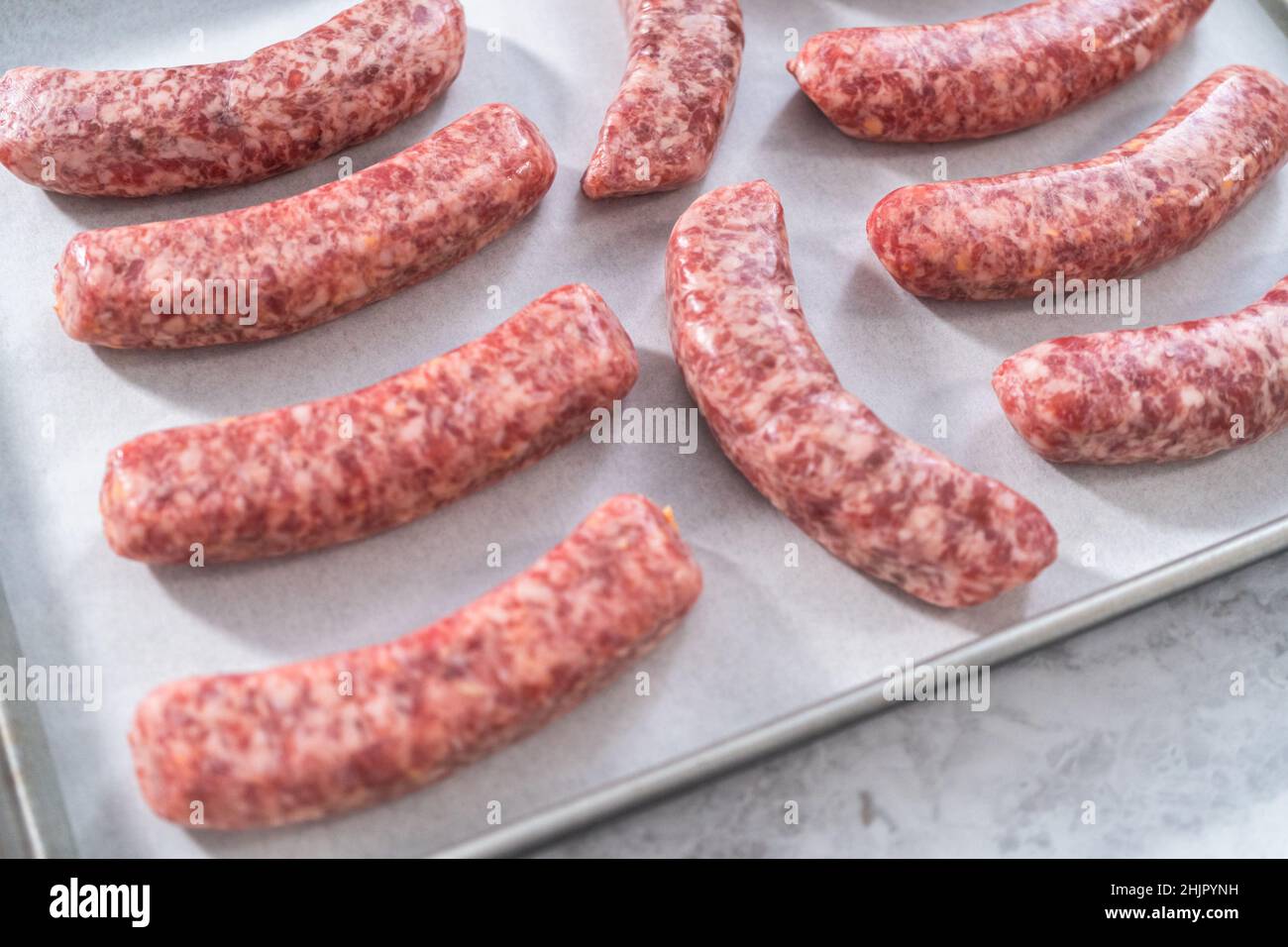 Raw beer bratwursts on a baking sheet lined with parchment paper ready ...