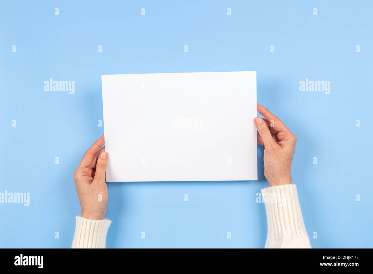 Female hands holding blank white paper sheet on light blue background ...