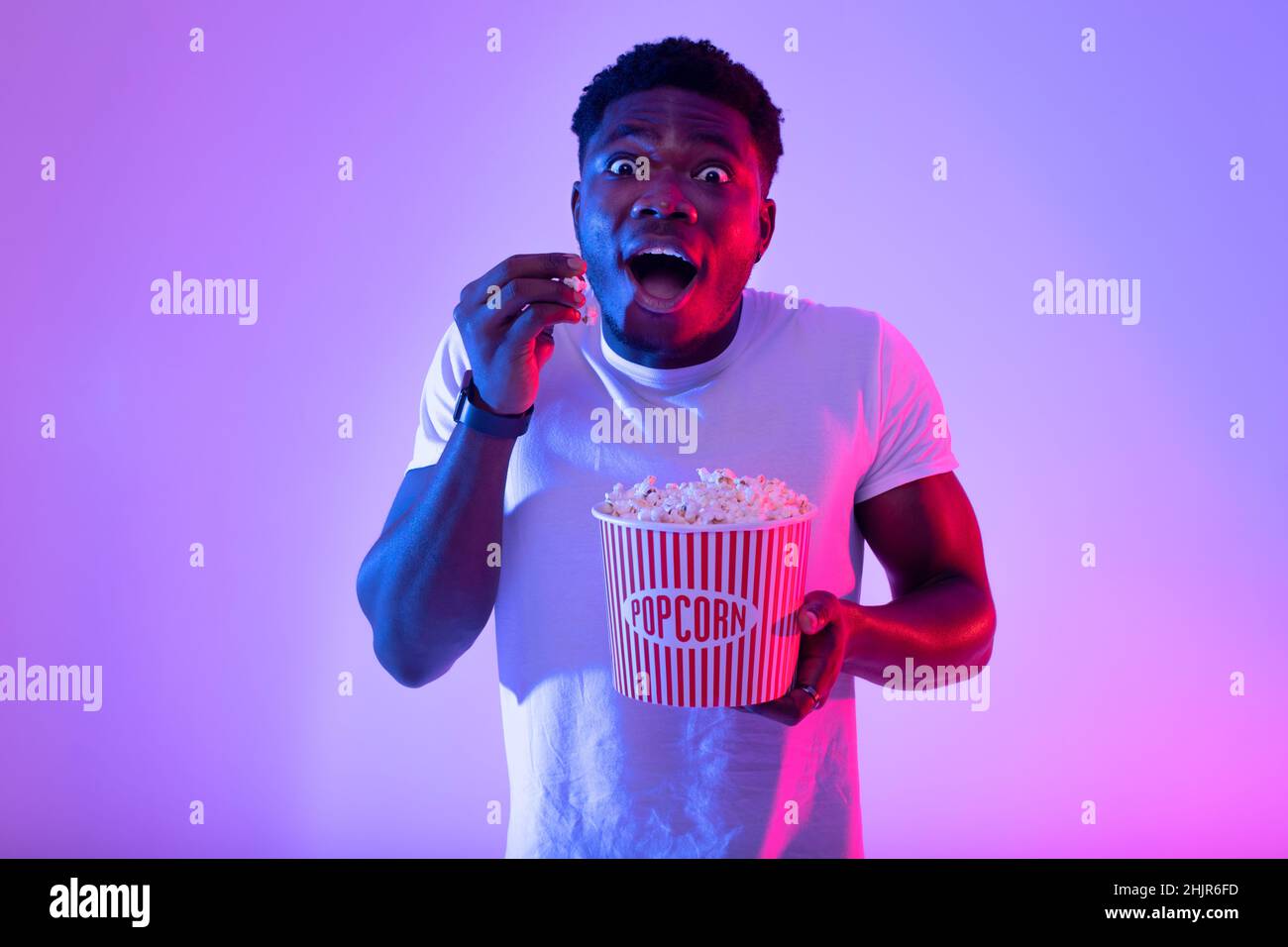 Portrait of excited young black guy eating popcorn from bucket ...