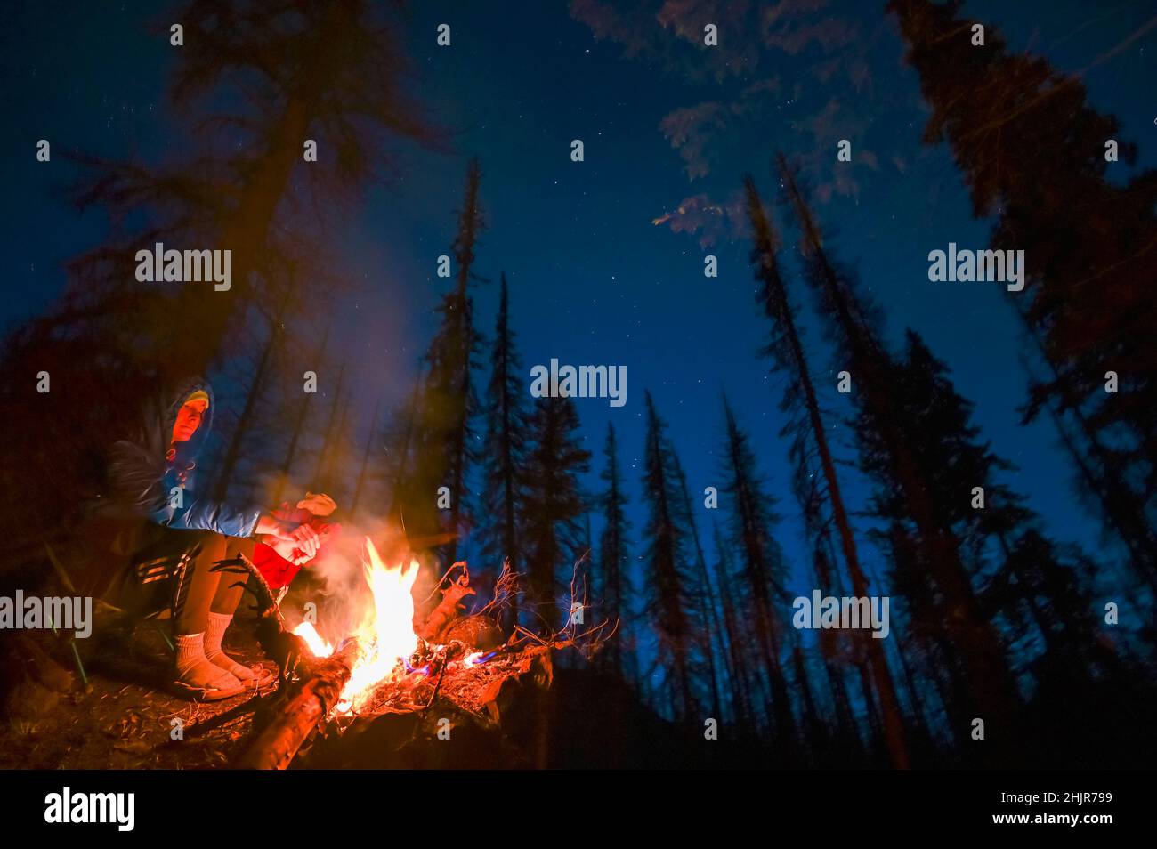Female camper staying warm next to campfire Stock Photo - Alamy