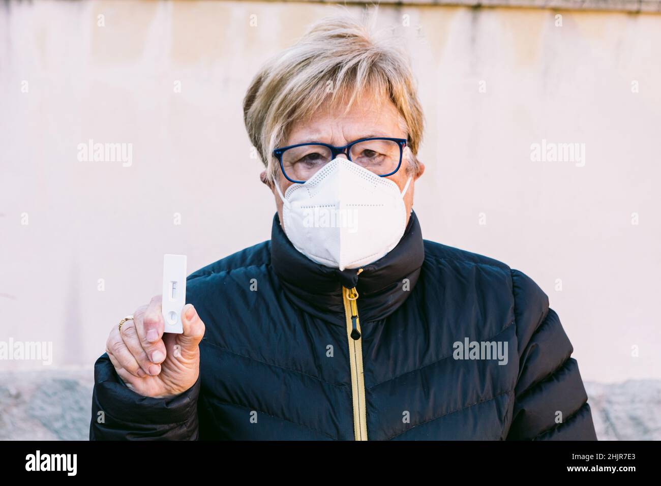Elderly lady on the street, wearing a white mask, with a negative ...