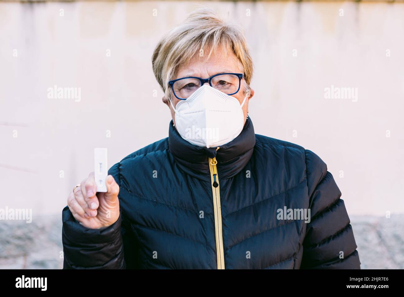 Elderly lady on the street, wearing a white mask, with a negative ...