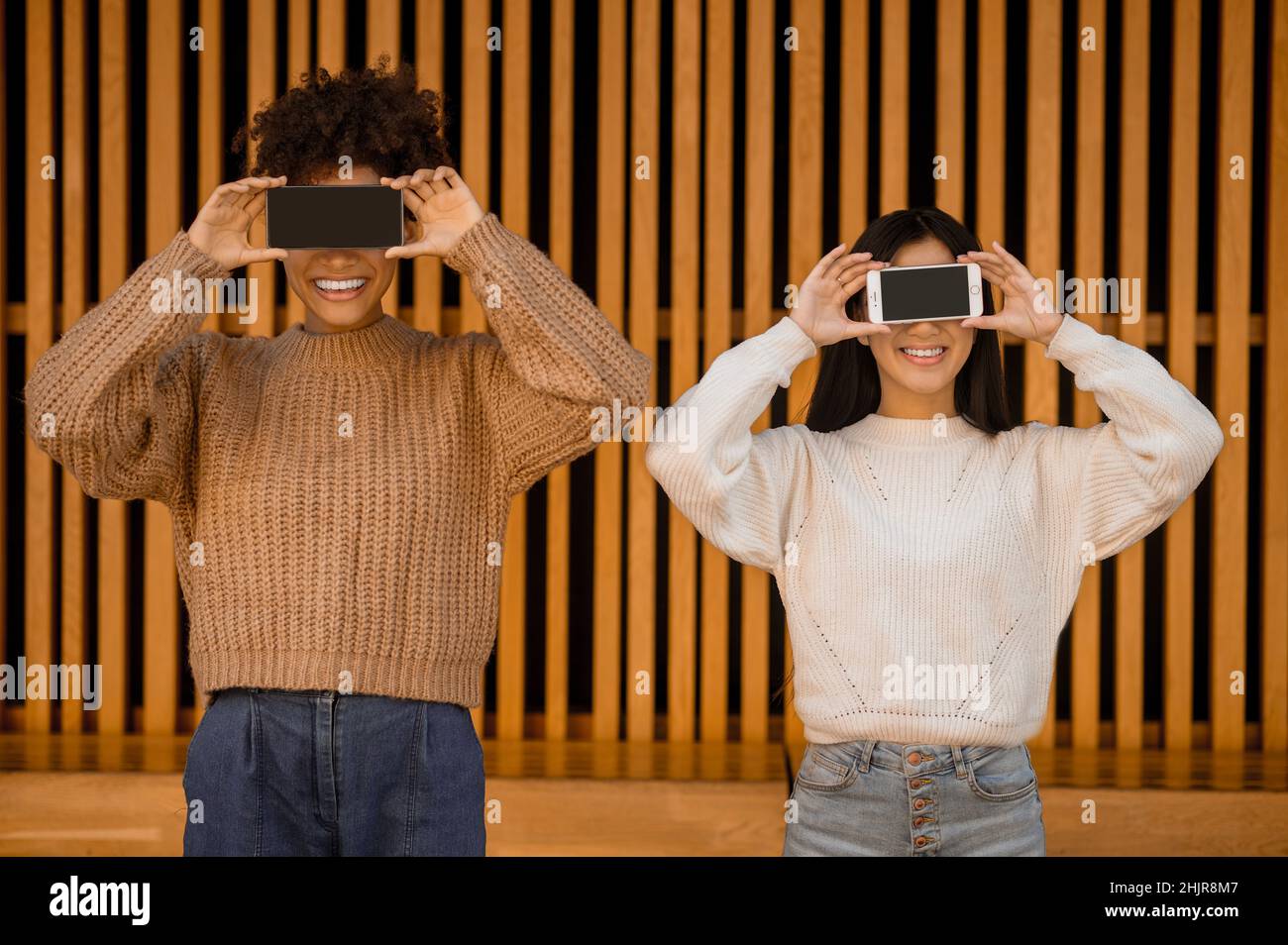 Two girls holding smartphones at eye level Stock Photo - Alamy