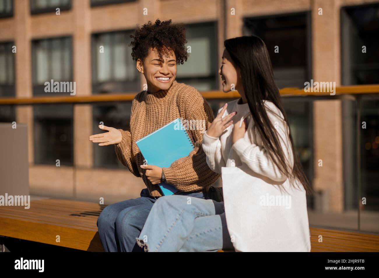 Two girls friendly communicating gesturing sitting on bench Stock Photo ...