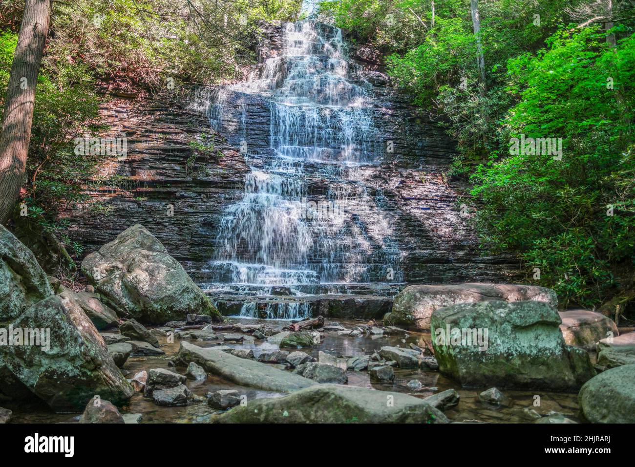 Large rock wall with cascading waterfall flowing into the shallow water ...