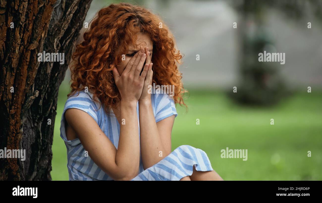 sad young woman with red hair covering face while crying in park Stock ...