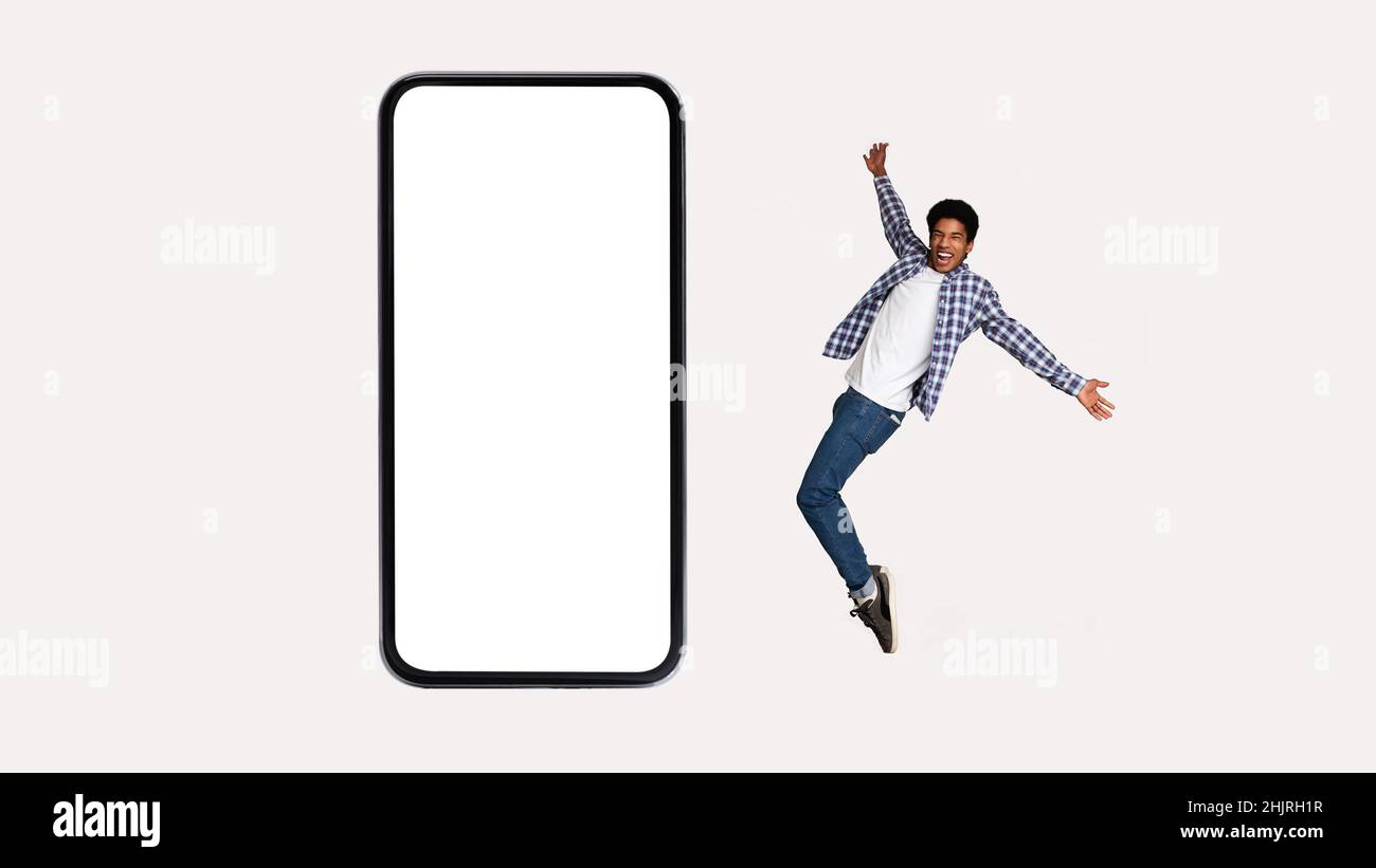 Happy Black Guy Jumping Near Smartphone Empty Screen, Gray Background ...