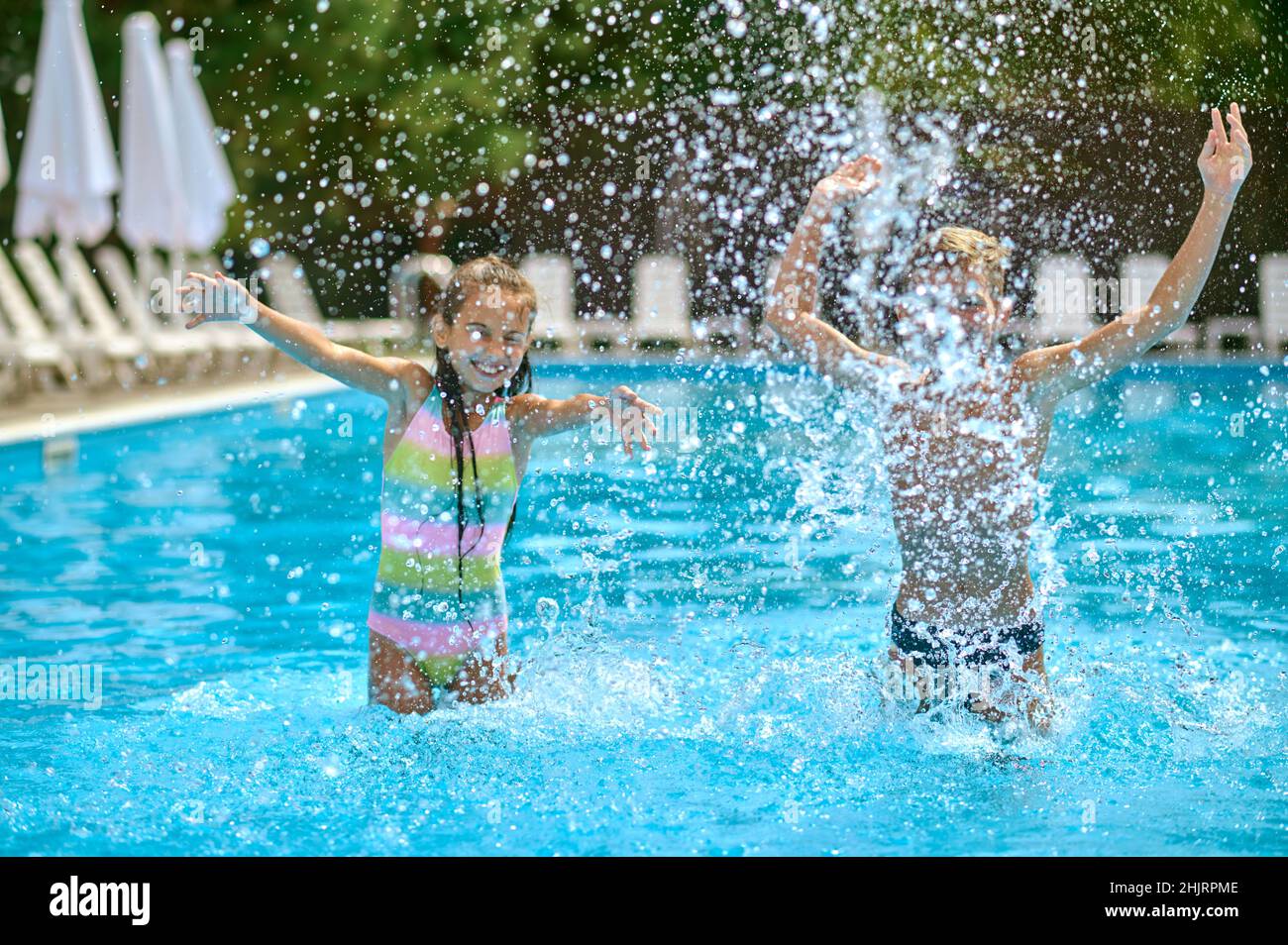 Children splashing water on camera while standing in pool Stock Photo ...