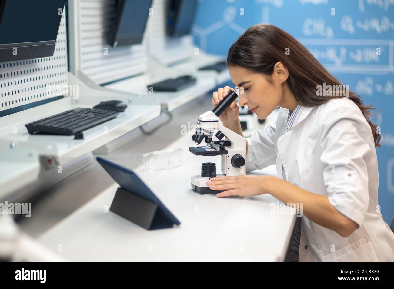 Woman sideways to camera looking through microscope Stock Photo - Alamy