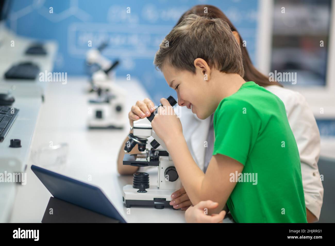 Boy looking through microscope near sitting teacher Stock Photo - Alamy