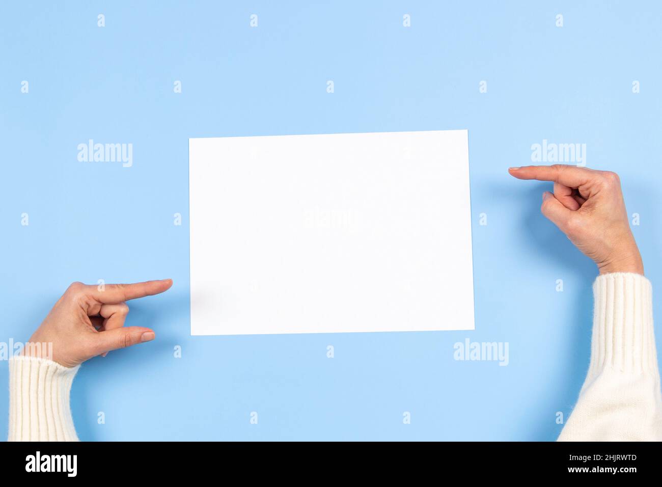 Female hands pointing to blank white paper sheet on light blue ...