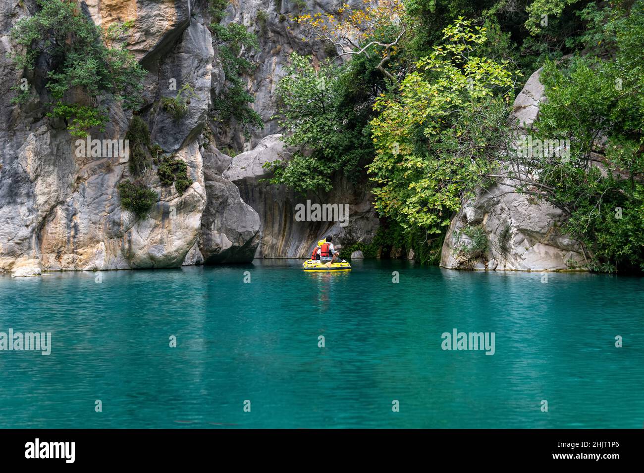tourists on an inflatable boat float down a rocky canyon with blue ...