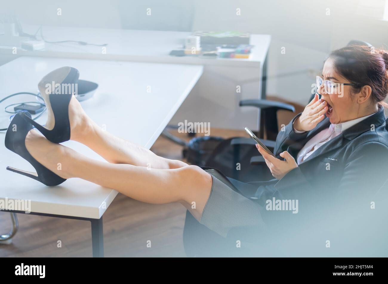 Business woman folded her legs on the desk and yawns. Boredom at work ...