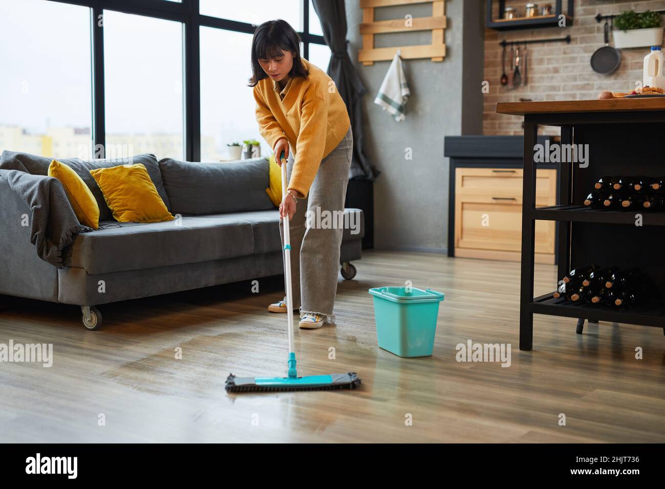 Full length portrait of young Asian woman mopping floors while cleaning ...