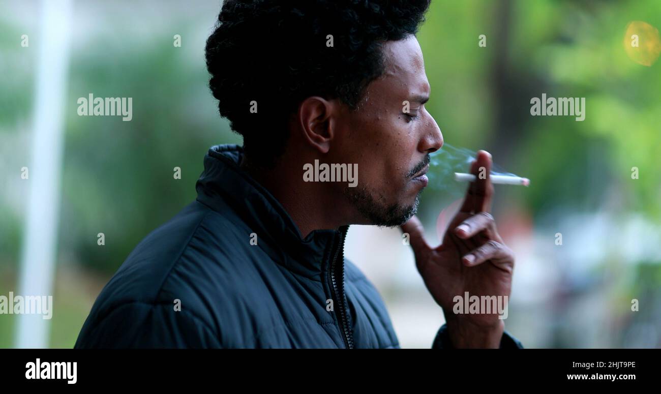 Pensive black african man smoking cigarette outdoors Stock Photo - Alamy