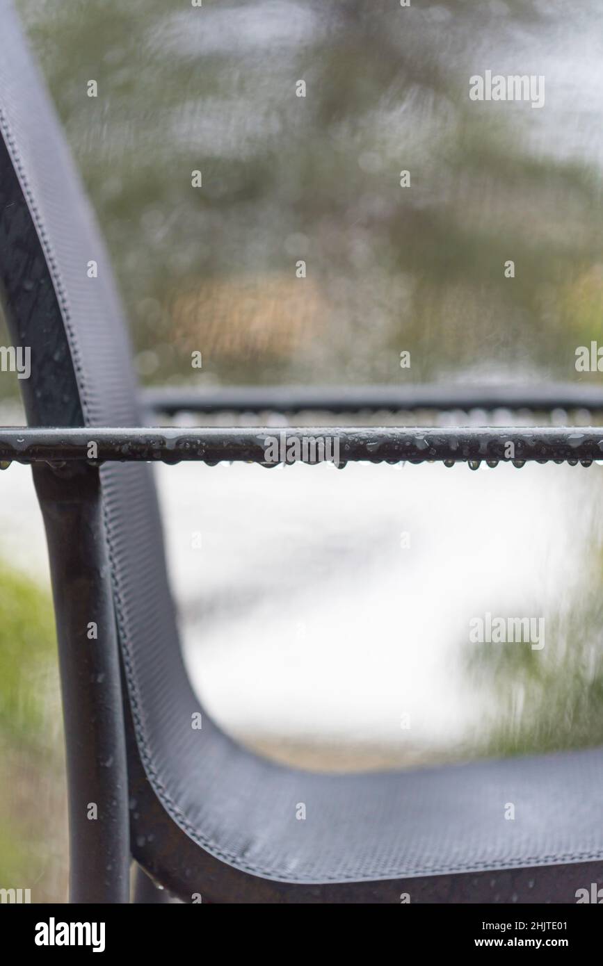 A concept image of an outdoor chair dripping wet in rain with a blurred ...