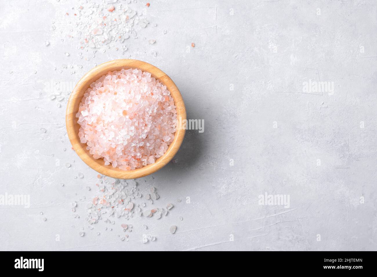 pink himalayan salt in a wooden bowl with scattered salt on a light ...