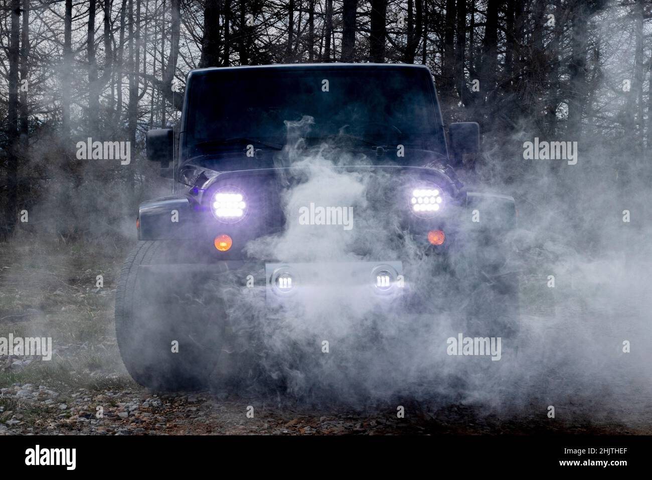 Black Jeep Wrangler on a back dirt road with headlights on and smoke ...