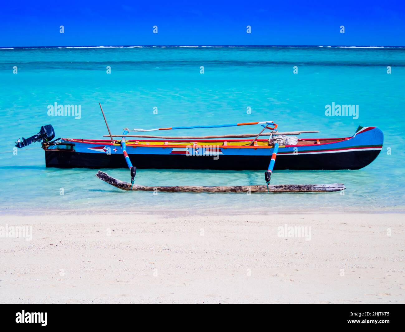 Multi-colored outrigger fishermen pirogue moored on turquoise sea of ...