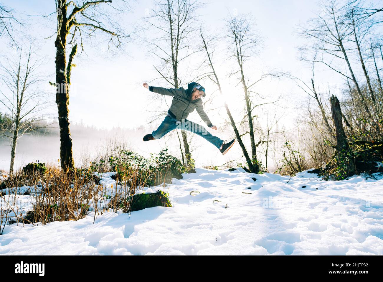 Straight on full length view of a man jumping off a log in winter Stock ...