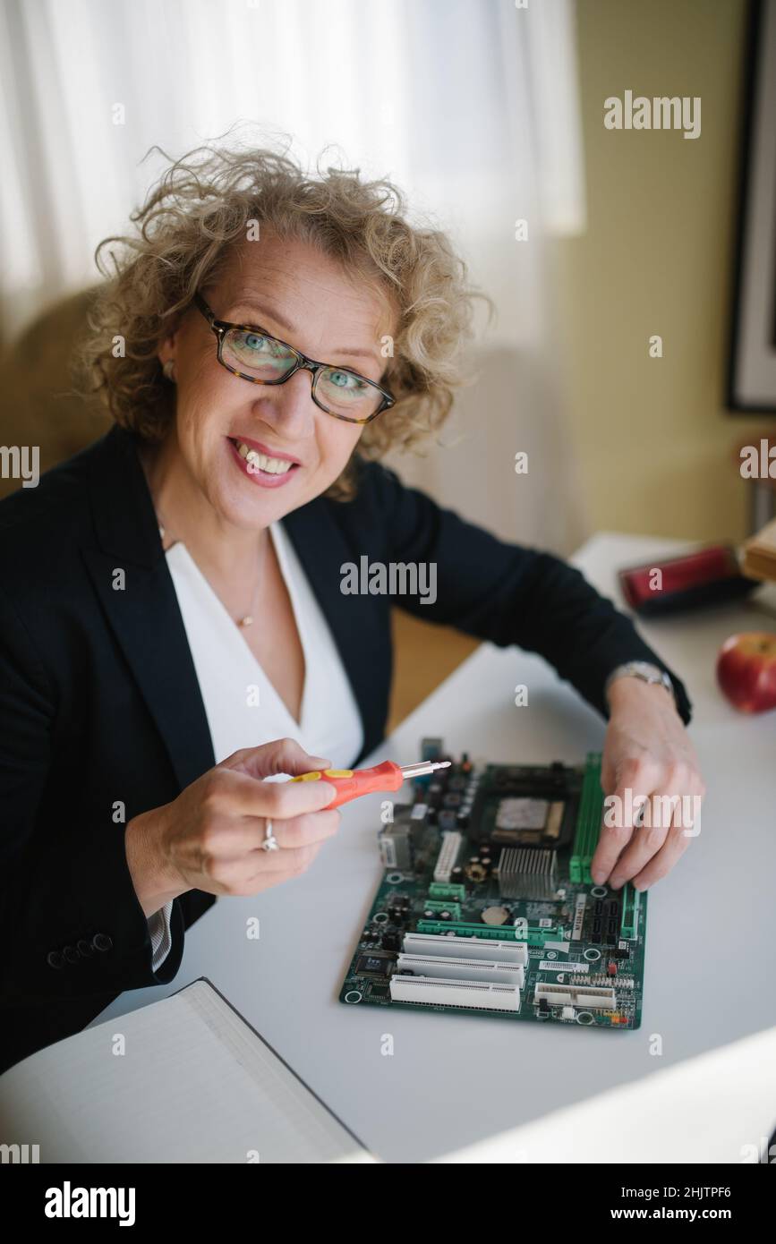 Middle-aged woman looking at camera and repair the computer component ...
