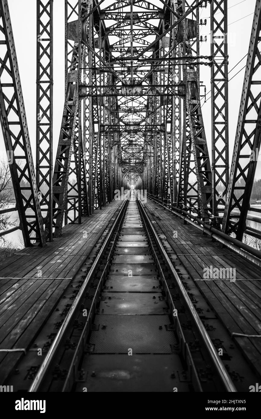 Vertical greyscale shot of a long metal bridge over the river Stock ...