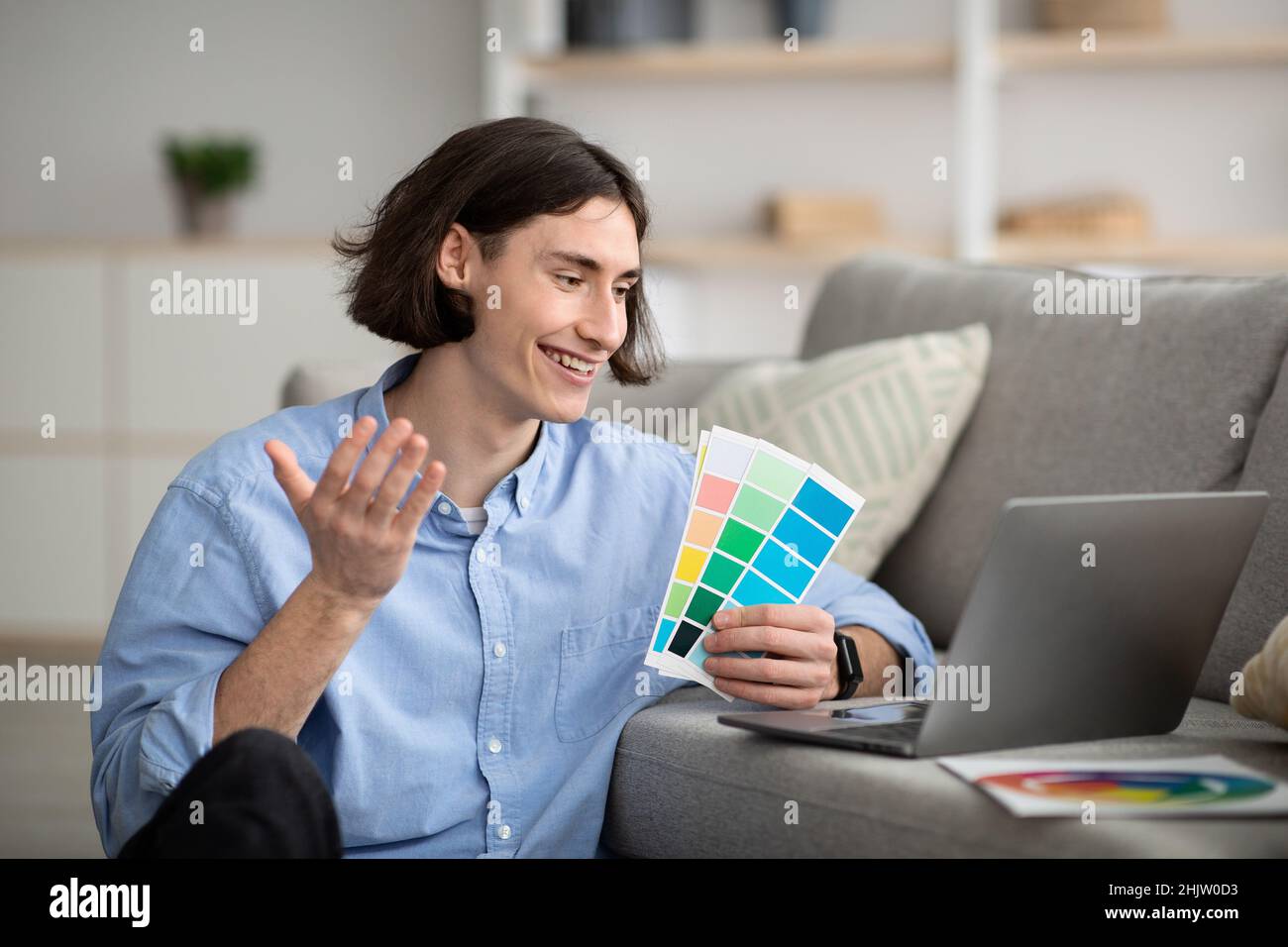 Young male freelancer holding color swatches in front of laptop ...