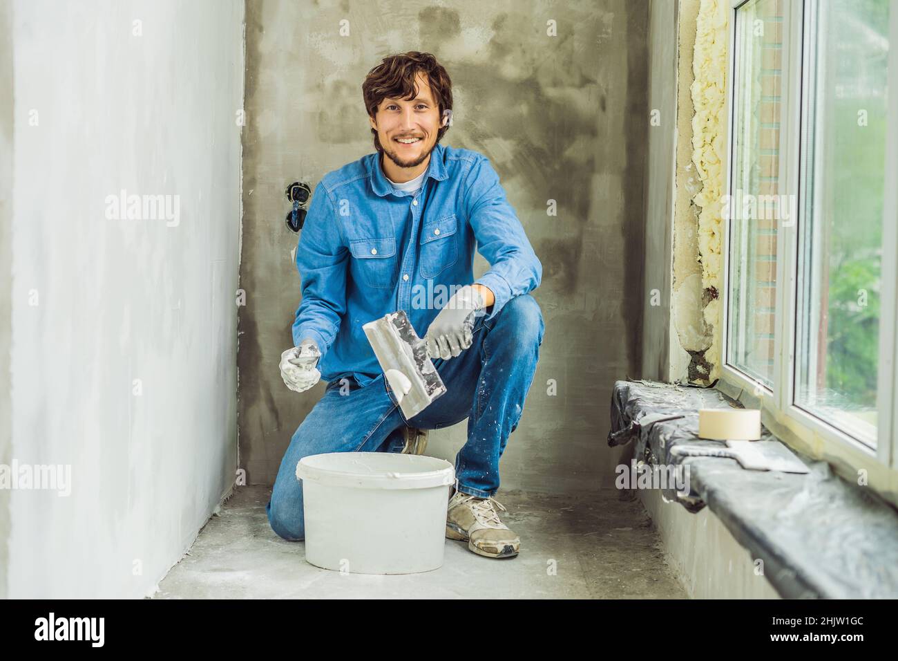 master is applying white putty on a wall and smearing by putty knife in ...