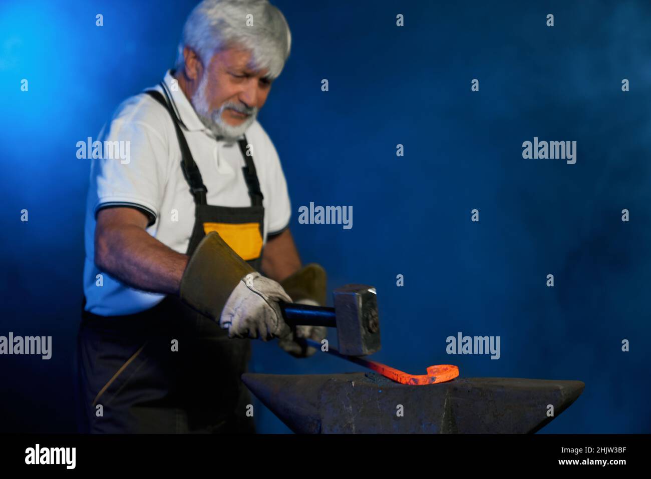 Skillful caucasian blacksmith with grey hair and beard forging molten ...
