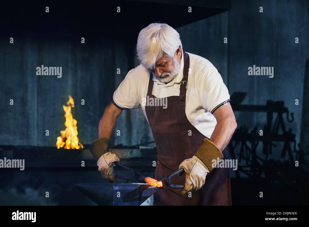 Strong mature man in protective gloves and apron bending molten steel ...