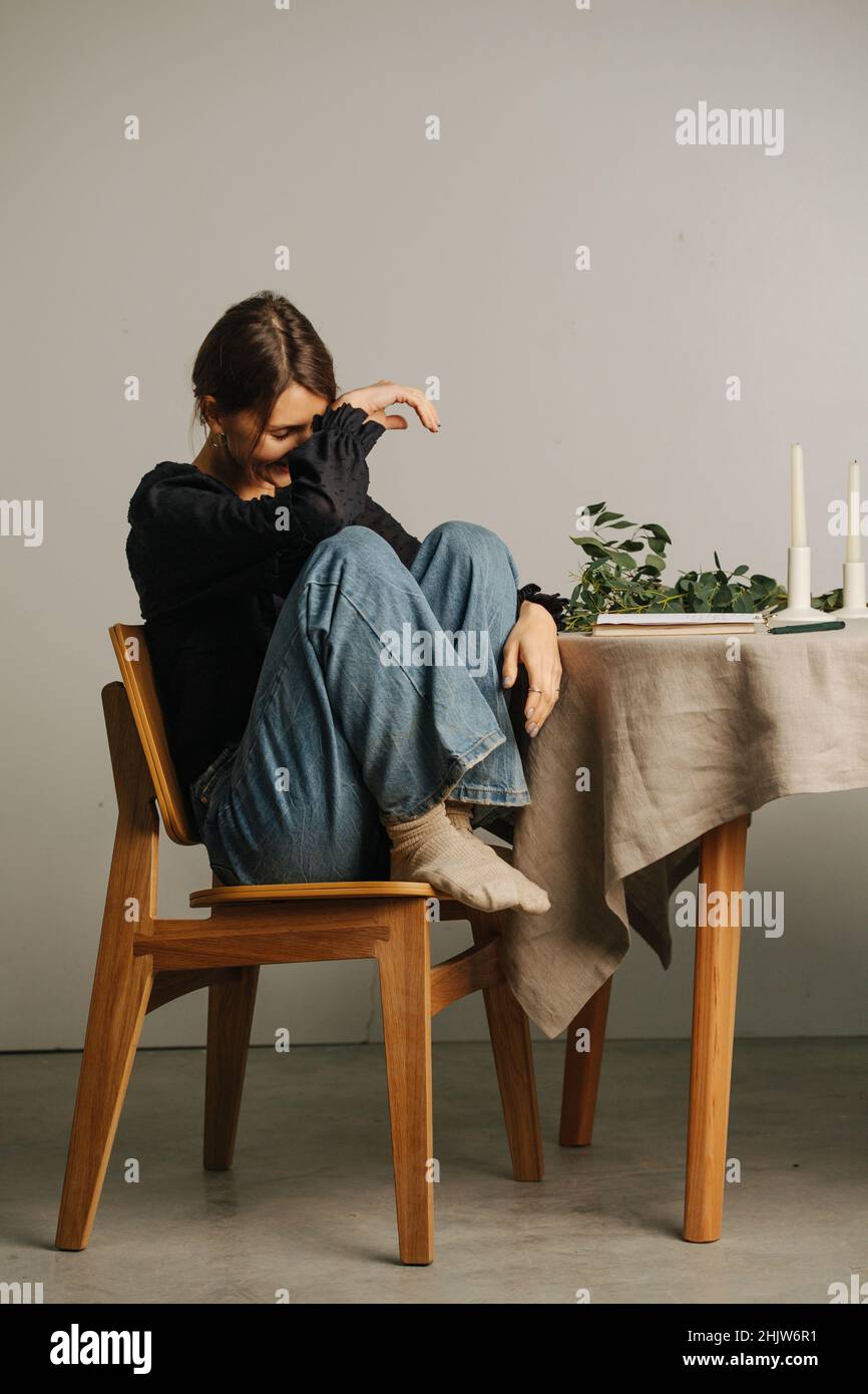 Resting laughing woman sitting with legs up on a chair next to a round ...