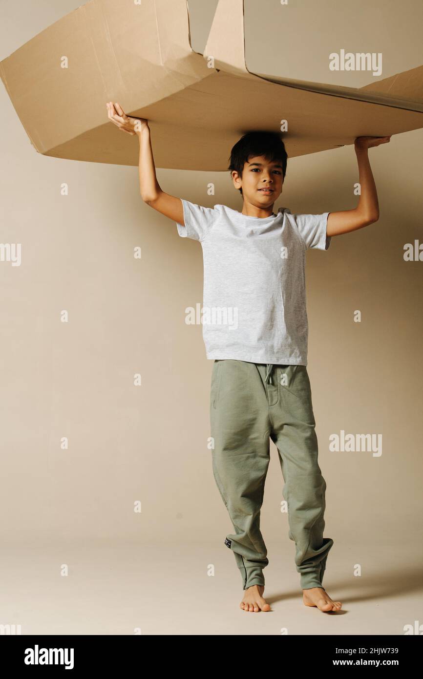 Cute indian boy holding cardboard box on his head twice his size ...