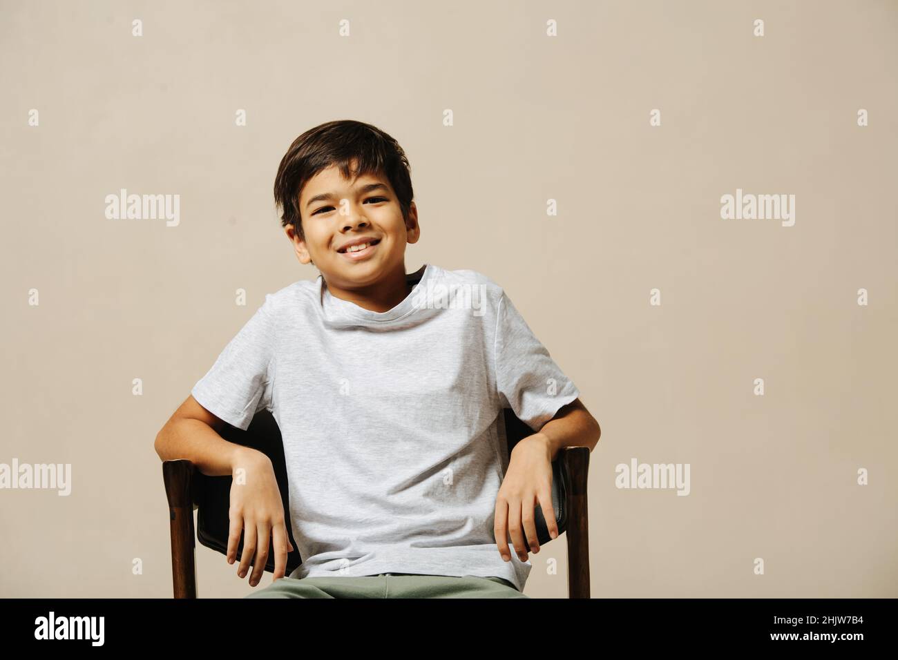 Smiling indian boy sitting on an armchair in a room over beige ...